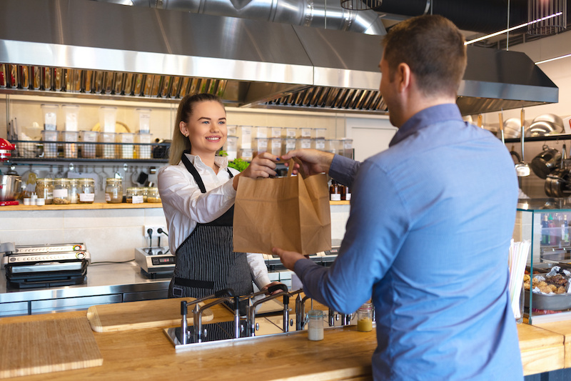 Smiling young waiter giving food order to man client at small fast food ...